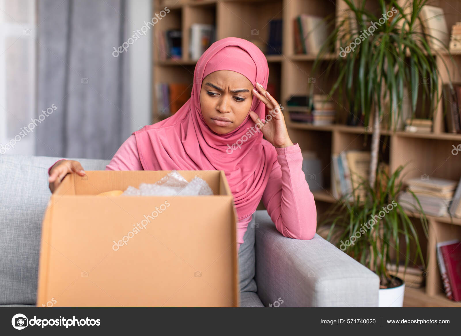Wrong item. Upset black muslim lady looking at open parcel with despair ...