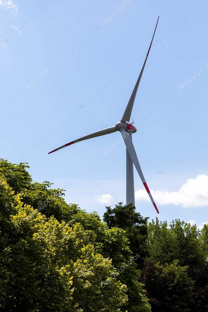 A vertical portrait of a windmill standing high above the trees in a ...