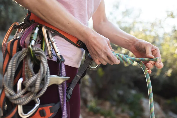 A rock climber prepares equipment for climbing, a woman holds a rope in ...