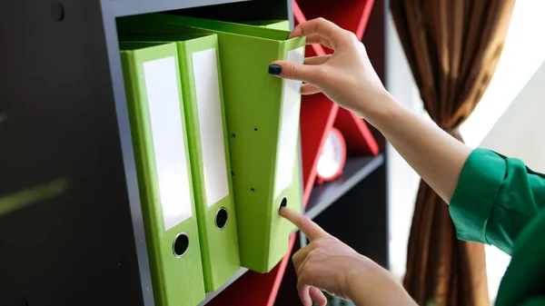 Close-up of woman taking off green folder with documents from shelf ...