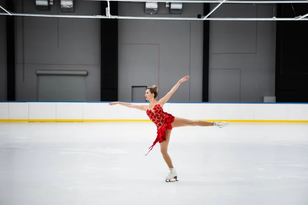 full length of figure skater in red dress performing camel spin in ...
