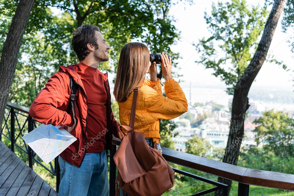 Sonriente turista sosteniendo mapa cerca de la novia con prismáticos en ...