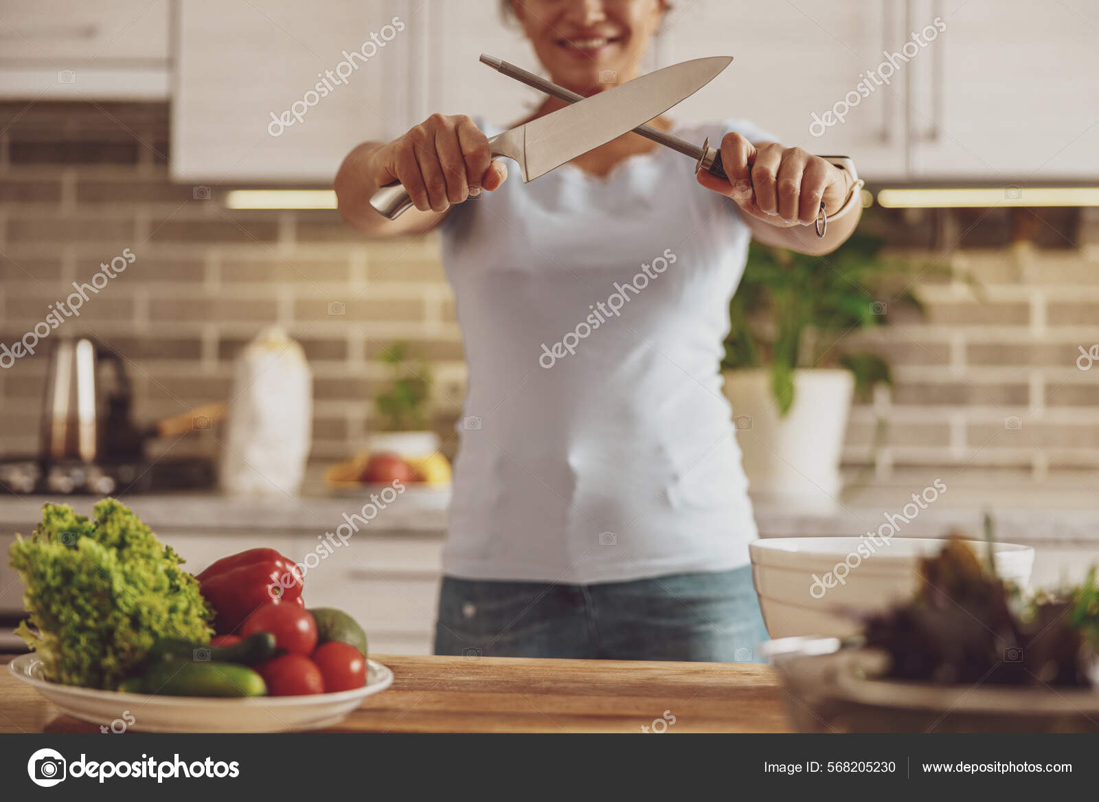 A housewife sharpens a knife standing at a table against the background ...