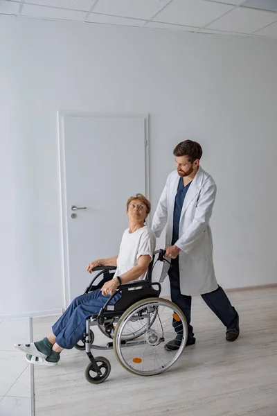 Professional male doctor carrying patient on wheelchair in medicine ...