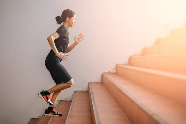 A beautiful woman runner is jogging up the steps under the sunlight ...