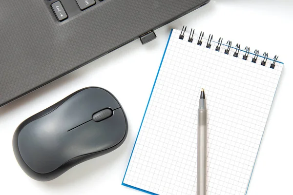 Computer wireless mouse, pen and notepad next to a laptop on a white ...
