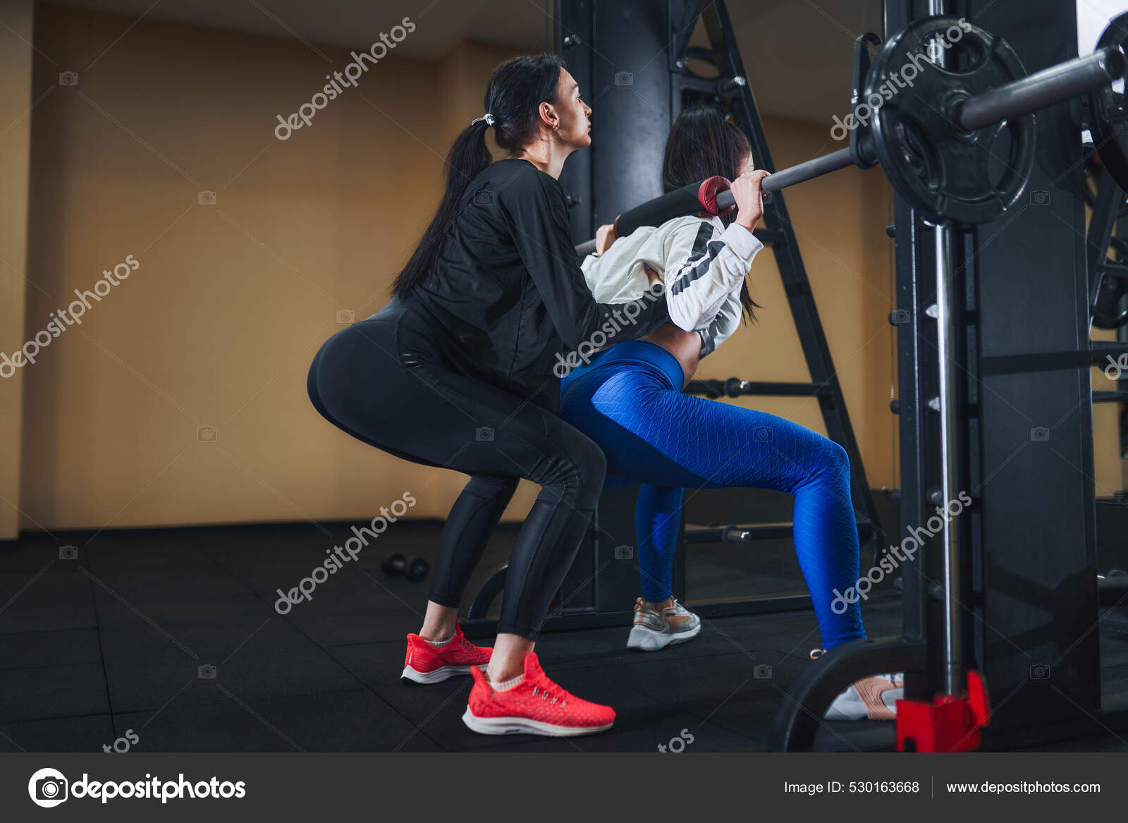 Young brunette woman working out legs with barbell in gym. personal ...