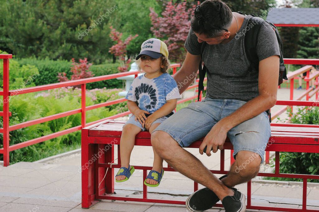Riendo cauc sico padre e hijo sentado en el banco en el soleado parque. Relaci n familiar y ...