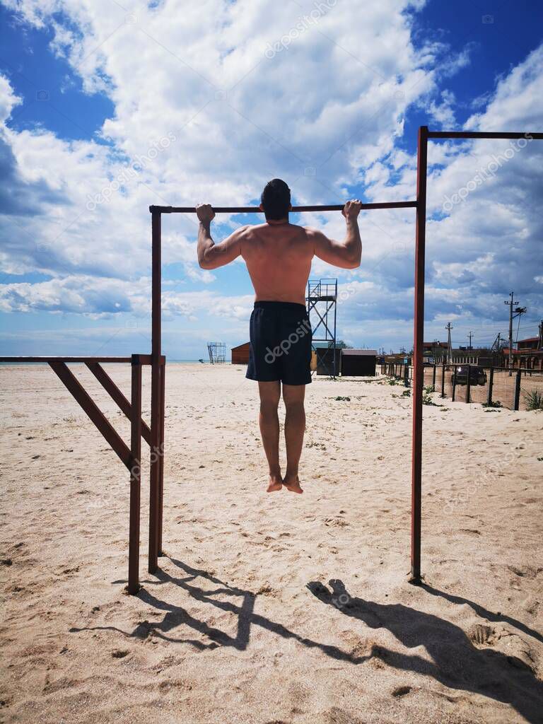 Rear view portrait of a young man in shorts doing pull-ups on the ...
