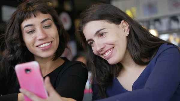 Two young women looking at smartphone device screen smiling. Female ...