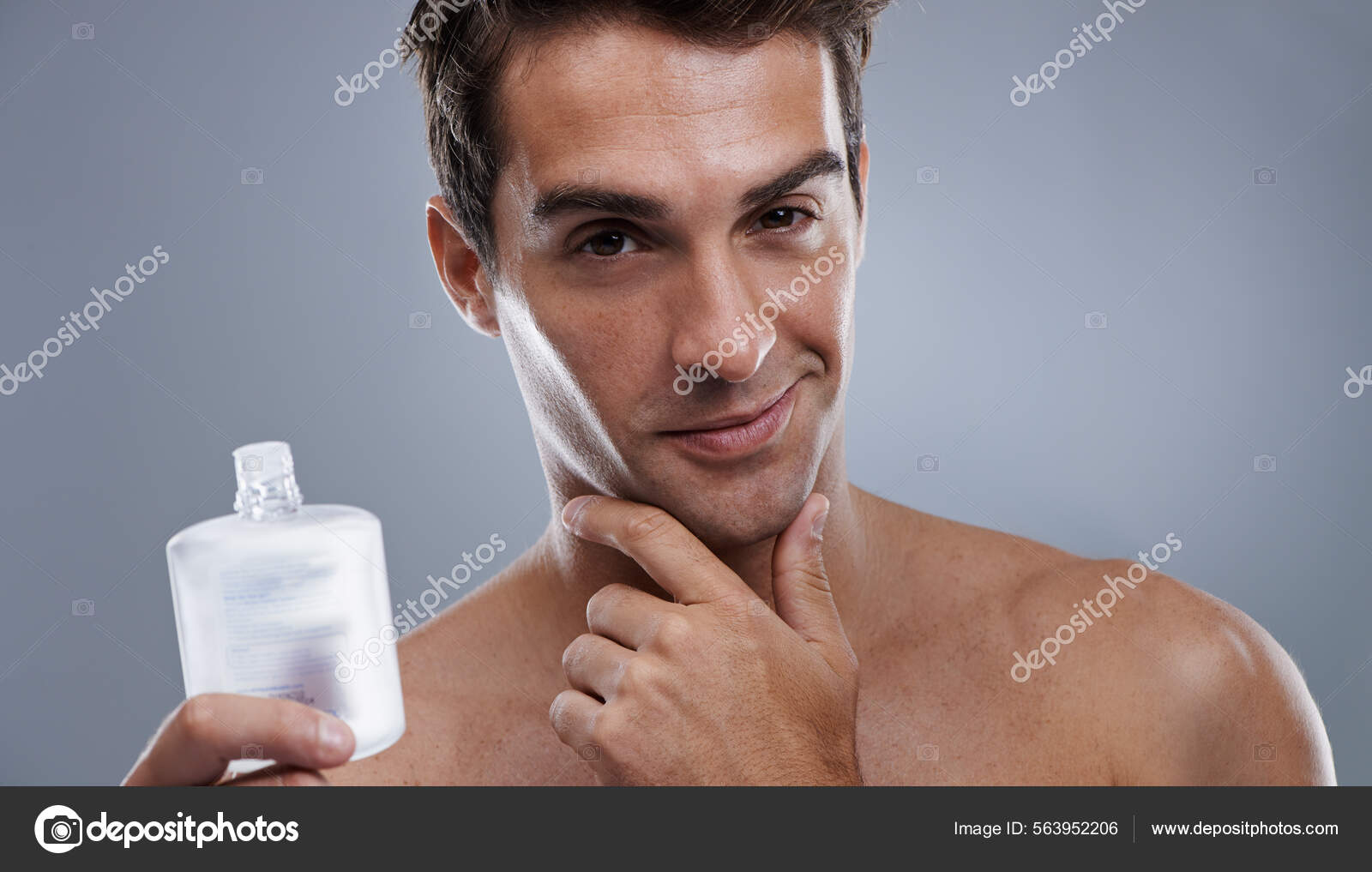 He always looks and smells great. Studio shot of a handsome young man applying aftershave to his ...
