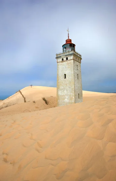 Lighthouse on a sand dune by the sea against a blue sky. Mysterious old ...