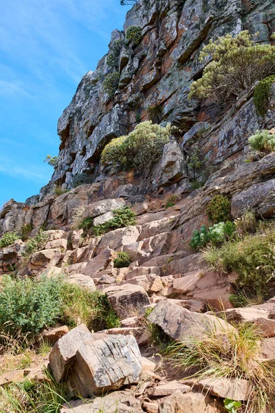 Rocky trail on a mountain with plants and grass against clear blue sky ...