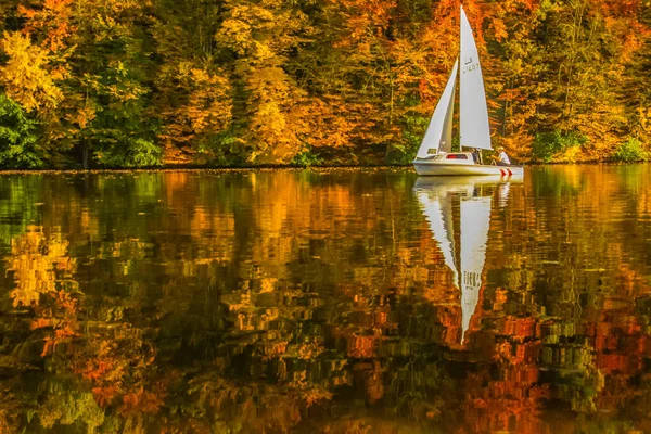 a sailboat and an autumn forest of red yellow and green autumn colors ...
