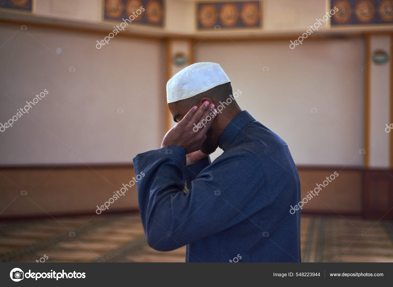 A young Muslim man prays in a mosque with his hands raised to his ...