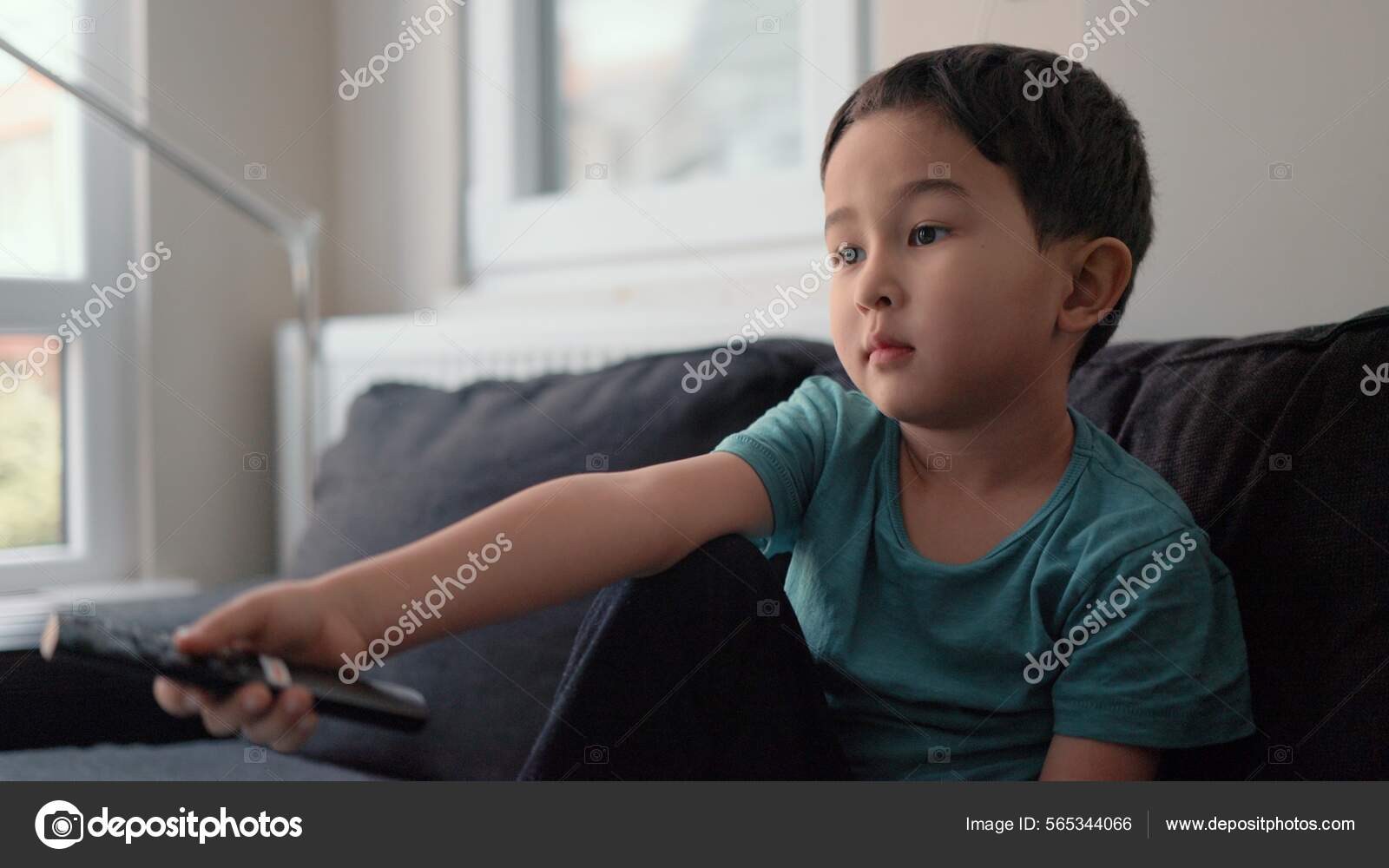 Little cute boy switch channels with remote control on TV at home ...