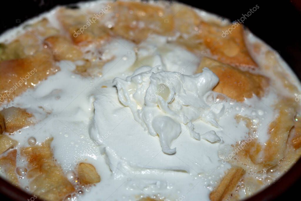 crema batida encima del budín de pan egipcio, leche en un tazón marrón ...