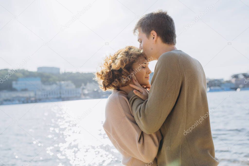 Un tipo guapo parado junto al mar besa a su novia en la frente ...