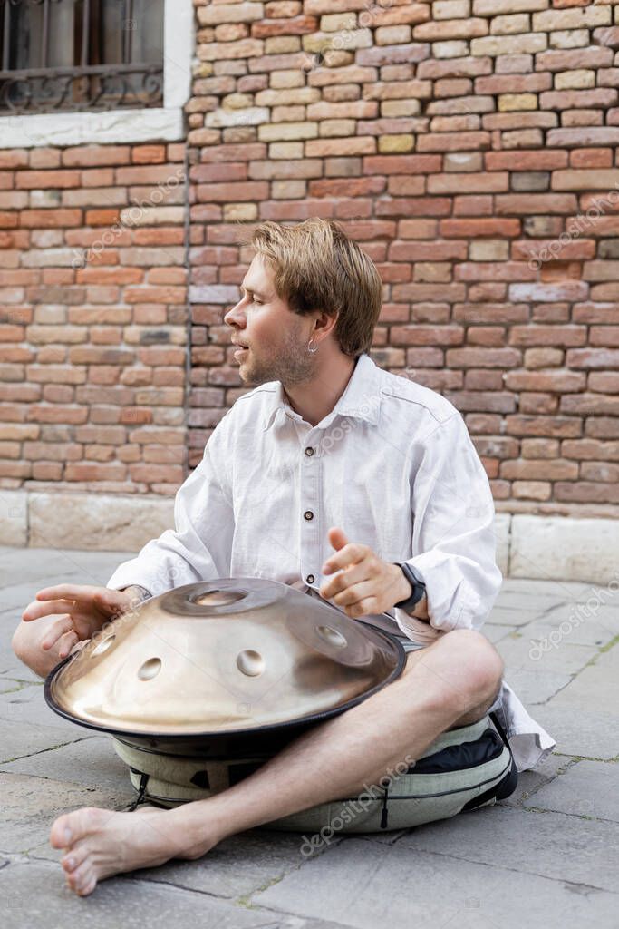 Side view of barefoot musician performing handpan on urban street in ...