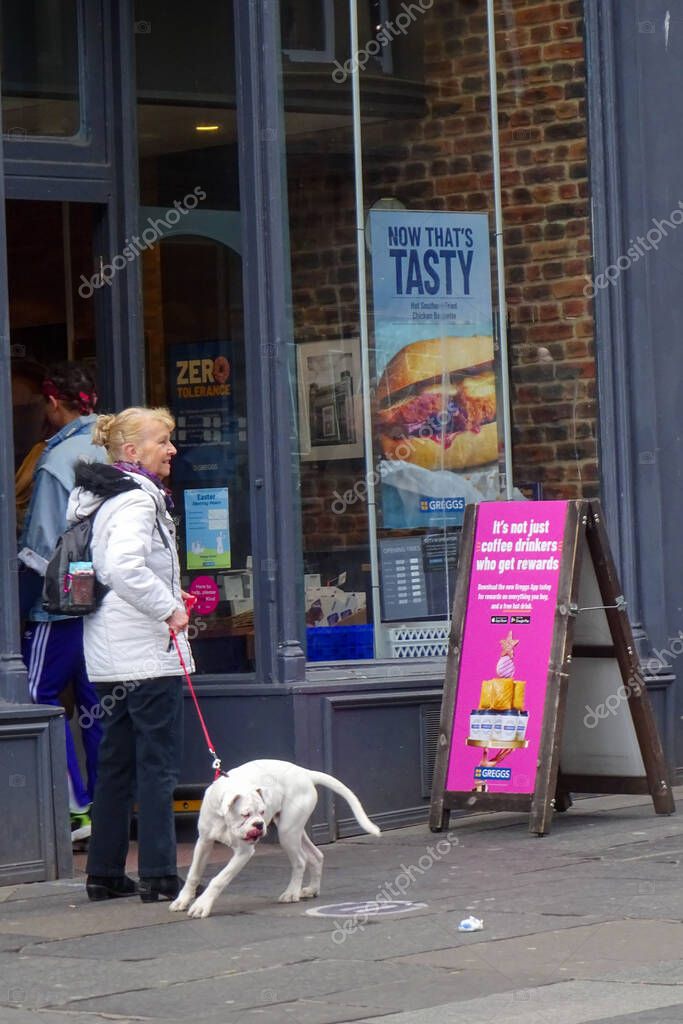 A woman stands outside a bakery with a sign, "Now That's Tasty" while ...