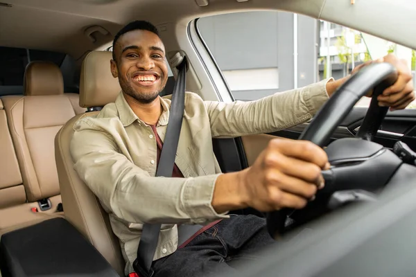 African American driver with hands on steering wheel looking at camera ...