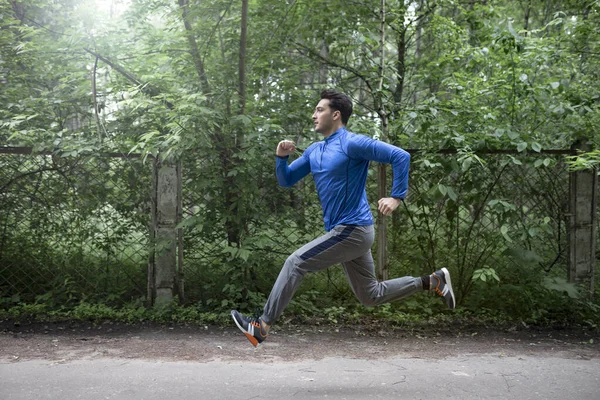 Young male athlete running fast on the road near wood - Stock Image ...