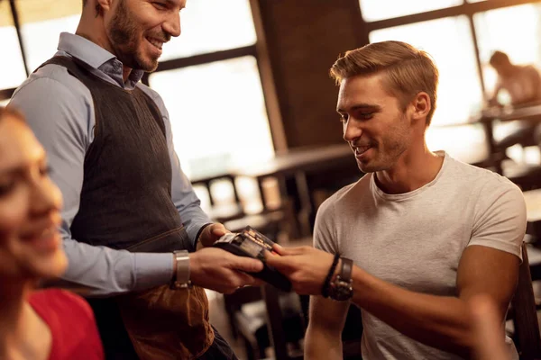 Young happy man paying waiter for restaurant check with contactless ...