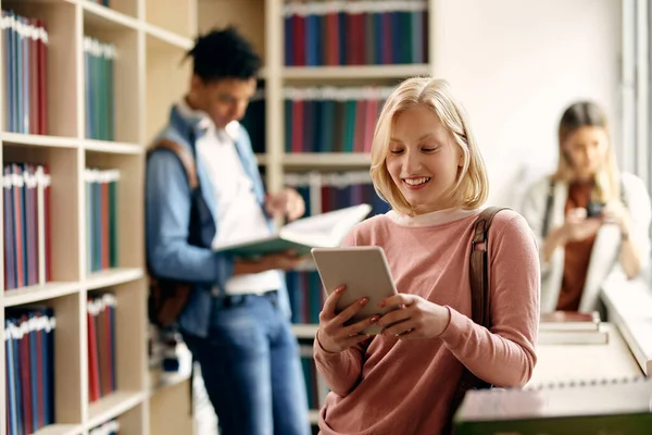 Happy college student using digital tablet while studying in a library ...