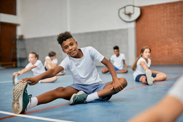 Happy black elementary student stretching his leg while warming up ...