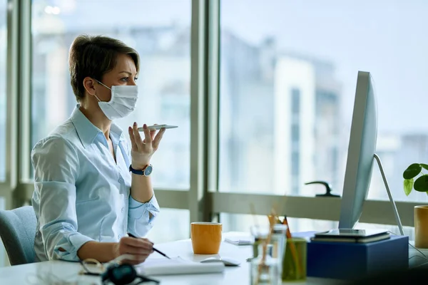 Businesswoman with face mask working on a computer while recording ...