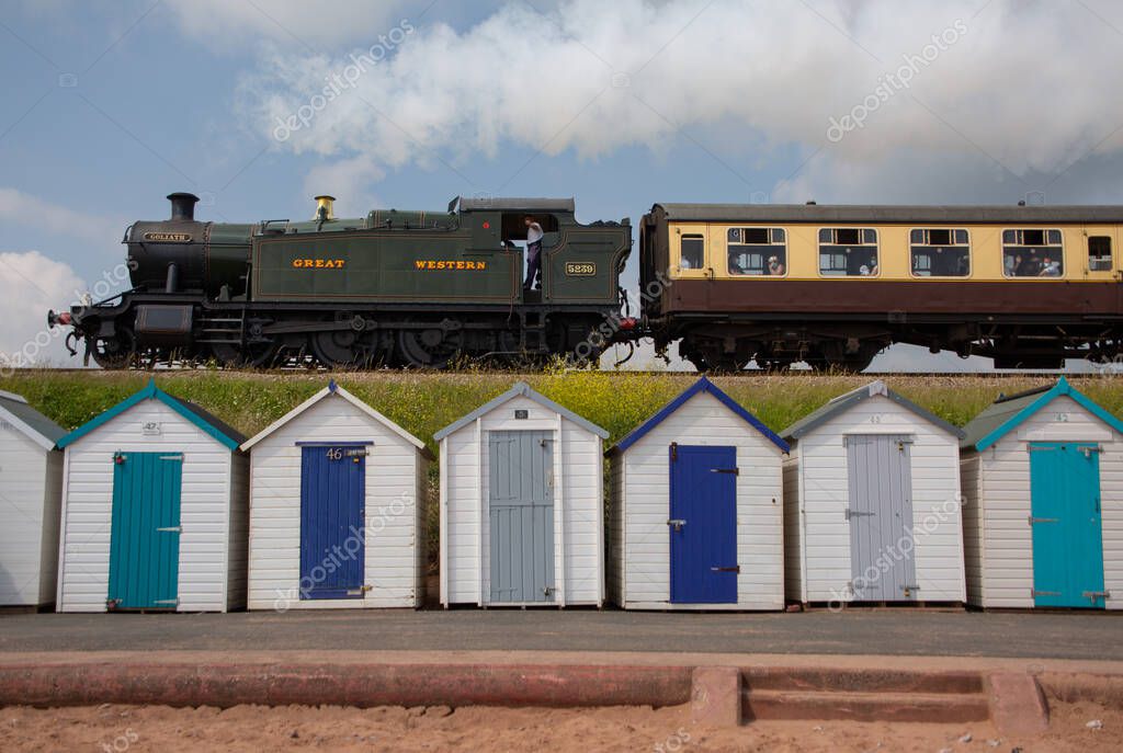 Great western rail steam train on tracks above colourful beach huts by ...