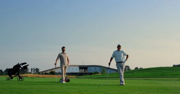 Two men enjoy golf on fairway field club. Golfing team practicing play ...