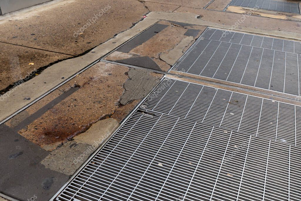 Superficie de una acera, múltiples áreas parcheadas y rejas metálicas ...